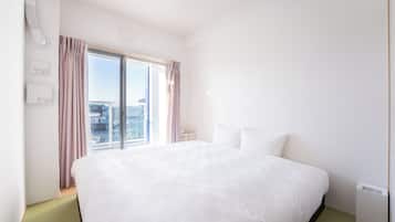 Quarto de hotel com uma cama grande, janela com cortinas, mesa de cabeceira e vista para a cidade.