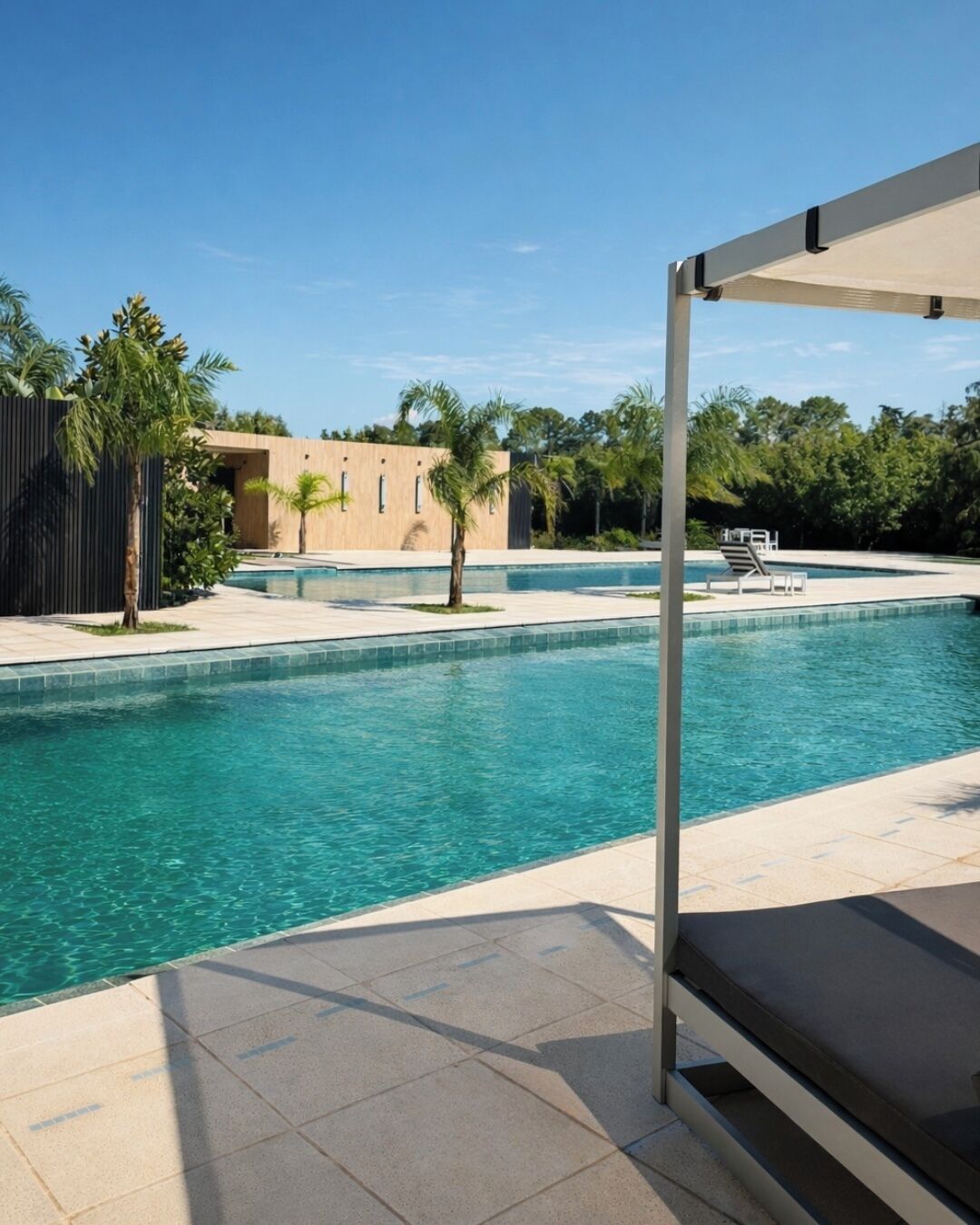 Piscina com água cristalina, cercada por palmeiras e um edifício moderno.