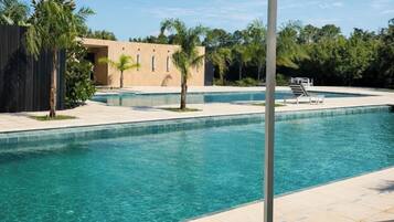 Piscina com água cristalina, cercada por palmeiras e um edifício moderno.
