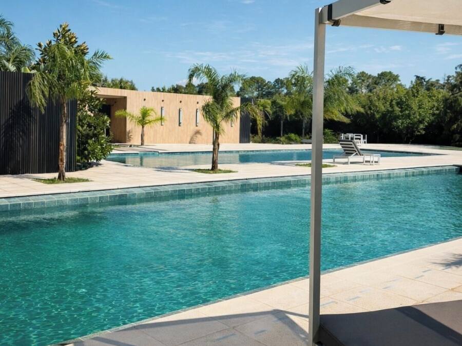 Piscina com água cristalina, cercada por palmeiras e um edifício moderno.