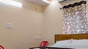 Quarto de hotel com cama de madeira, ventoinha no teto, ar condicionado e uma cadeira vermelha.