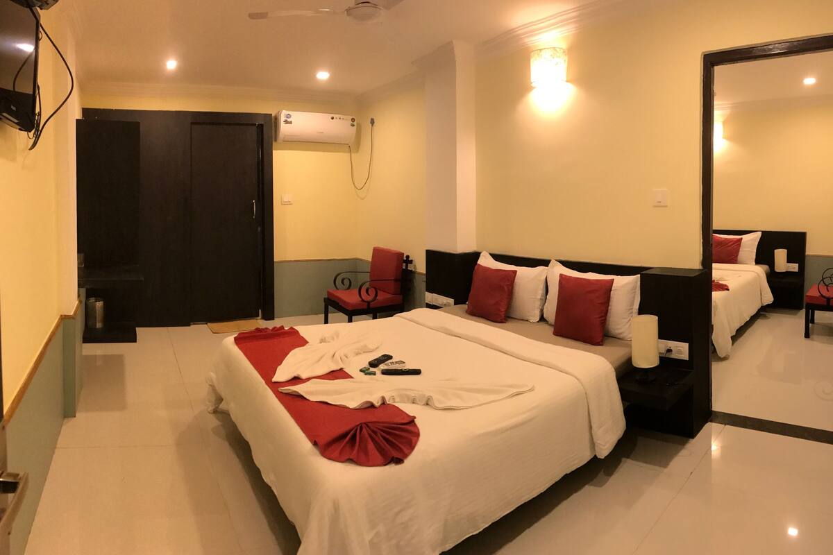 Quarto de hotel com uma cama grande, uma poltrona, mesa de cabeceira, espelho e aparelho de ar condicionado.
