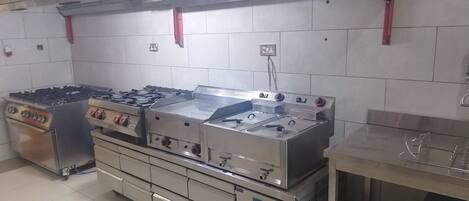 Cozinha industrial com eletrodomésticos de aço inoxidável, incluindo fogão, forno e coifa.