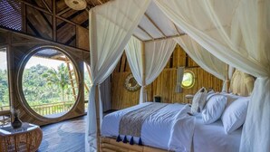 Uma cama com lençóis brancos, uma janela redonda e um tapete de palha.
