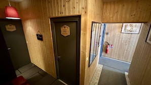 Um corredor revestido de madeira com uma porta identificada como “Local à Skis Poussettes”, um extintor de incêndio e um aviso com o código do WiFi.