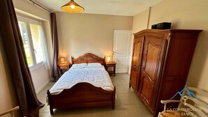 Quarto com cama de madeira, duas mesas de cabeceira com luminárias, um guarda-roupa e uma janela com cortinas.