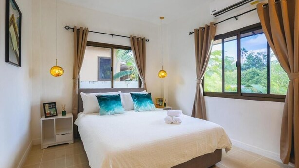 Quarto com uma cama grande, duas mesas de cabeceira, uma mesinha de apoio, janela com cortinas e vista para o verde lá fora.