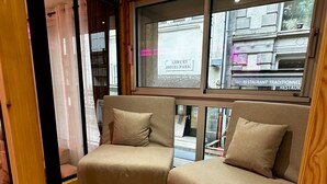 Um interior moderno com dois sofás bege, piso de madeira e uma grande janela com vista para a rua.