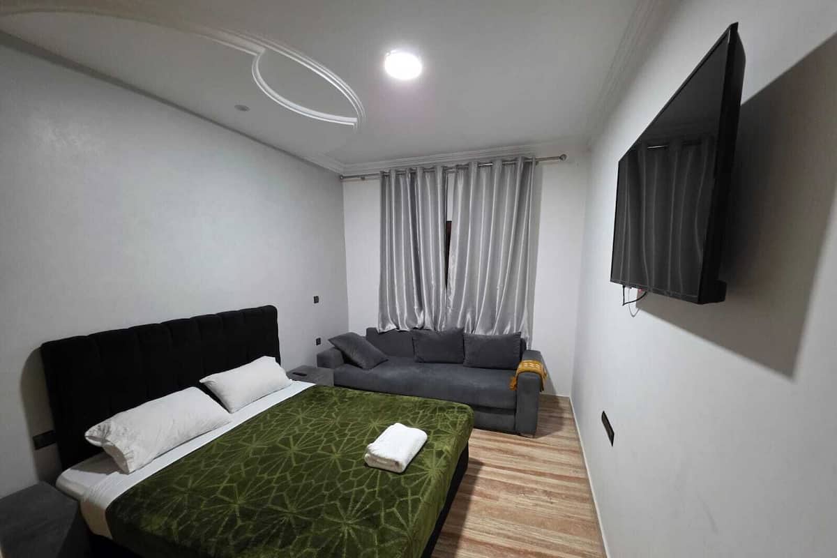 Um quarto moderno com cama, sofá, televisão e janela com cortinas.