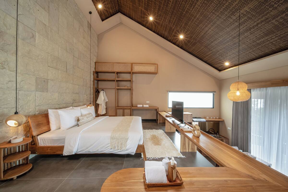 Um quarto moderno com uma cama grande, uma escrivaninha de madeira, uma televisão e uma parede de pedra.