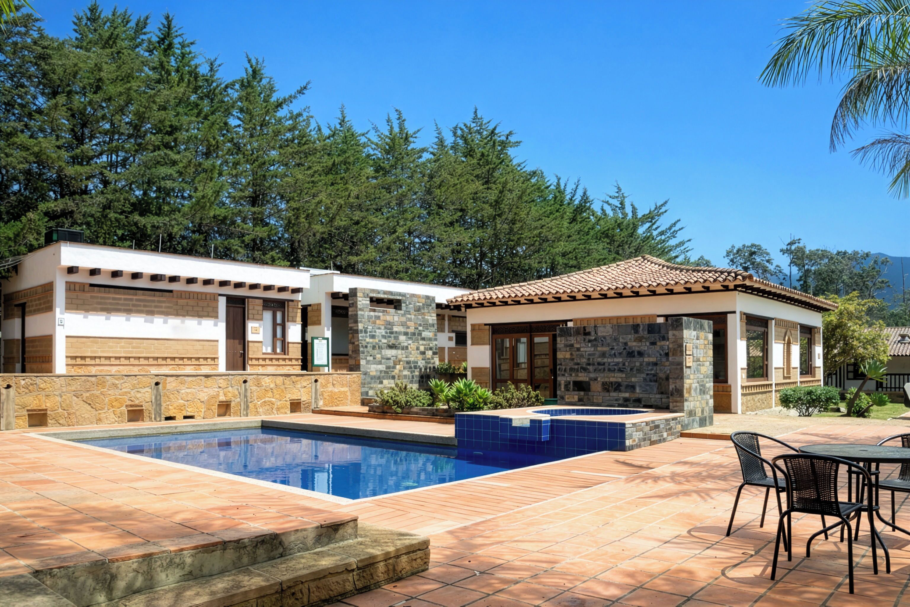 Uma área de piscina com um pátio, um espaço de estar coberto e um edifício com paredes de pedra e azulejos.