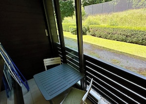 Varanda com mesa e cadeiras, vista para um jardim bem cuidado e uma cerca.