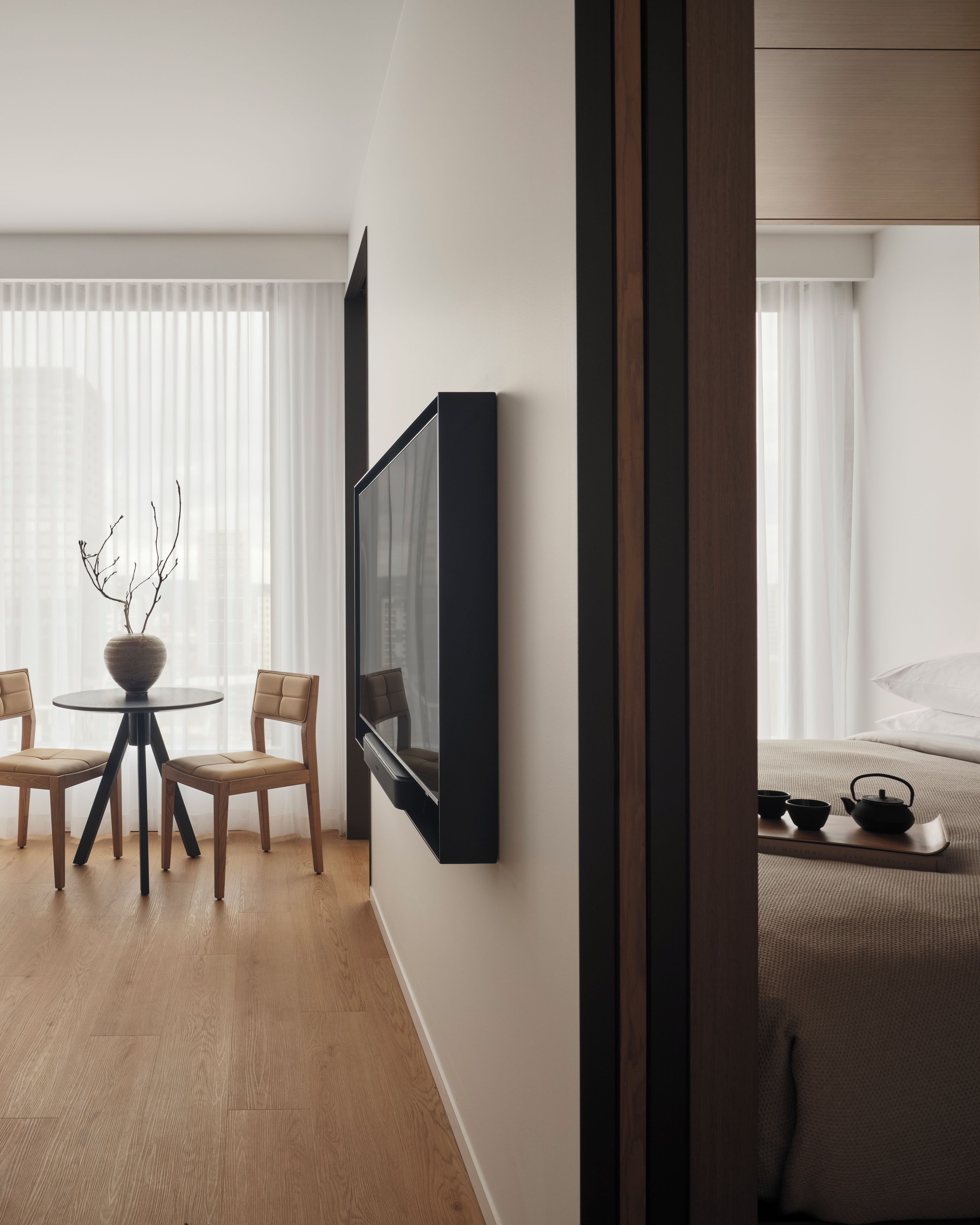 Quarto de hotel moderno com área de jantar, televisão e cama com bandeja de chá e bule.