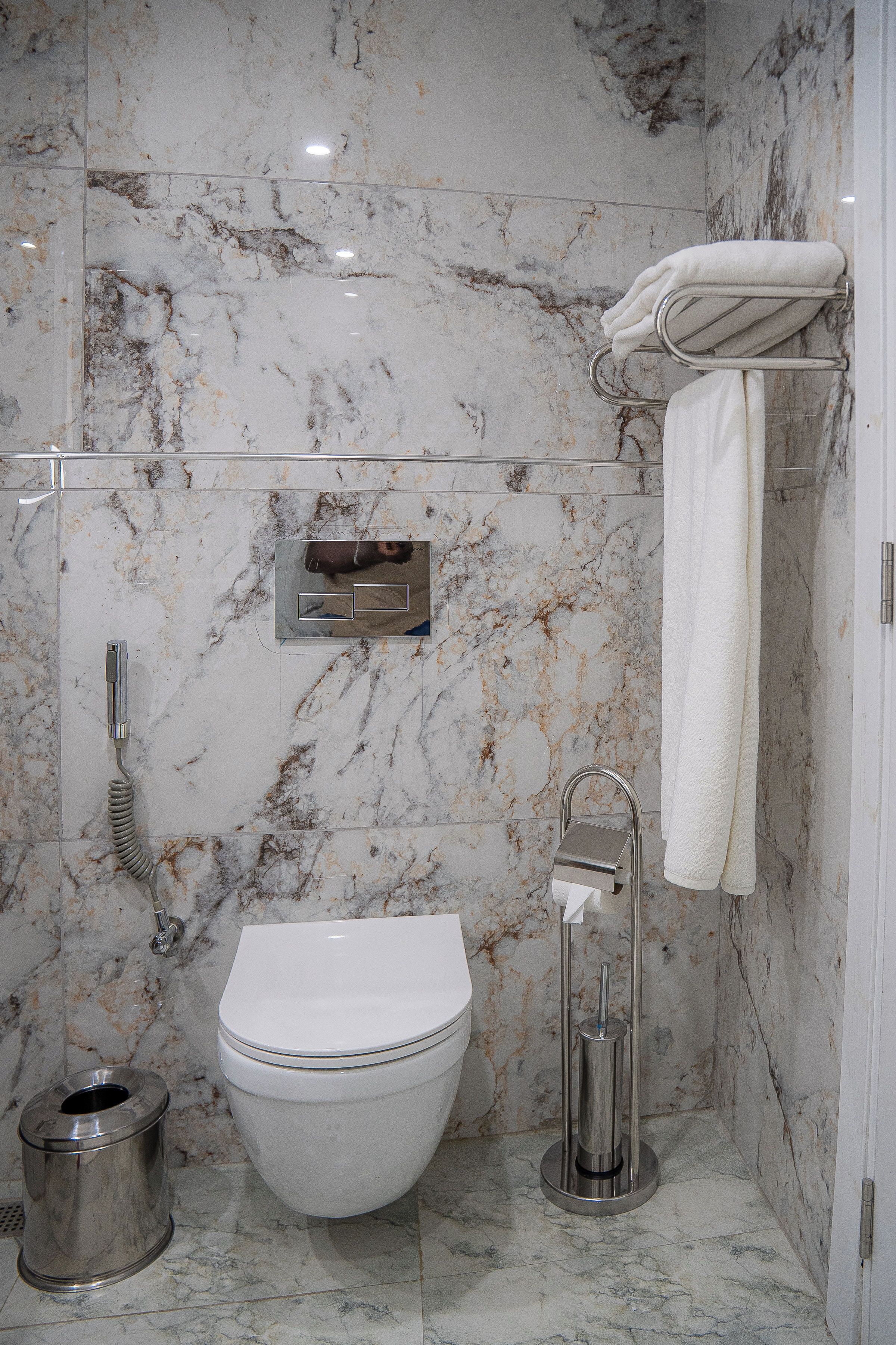 Casa de banho com soalho de mármore, sanita, bidé, um porta-toalhas e um cesto de lixo.