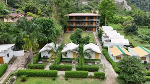 Um hotel com vários quartos tipo bangalô dispostos em fileiras, rodeado por vegetação exuberante e um edifício central com varandas.