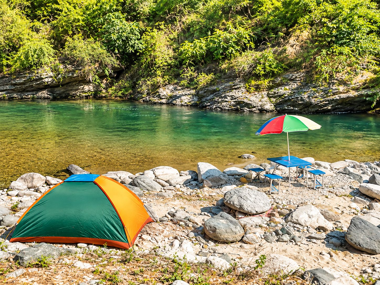 Um camping com tendas e uma mesa com cadeiras à beira de um rio calmo.