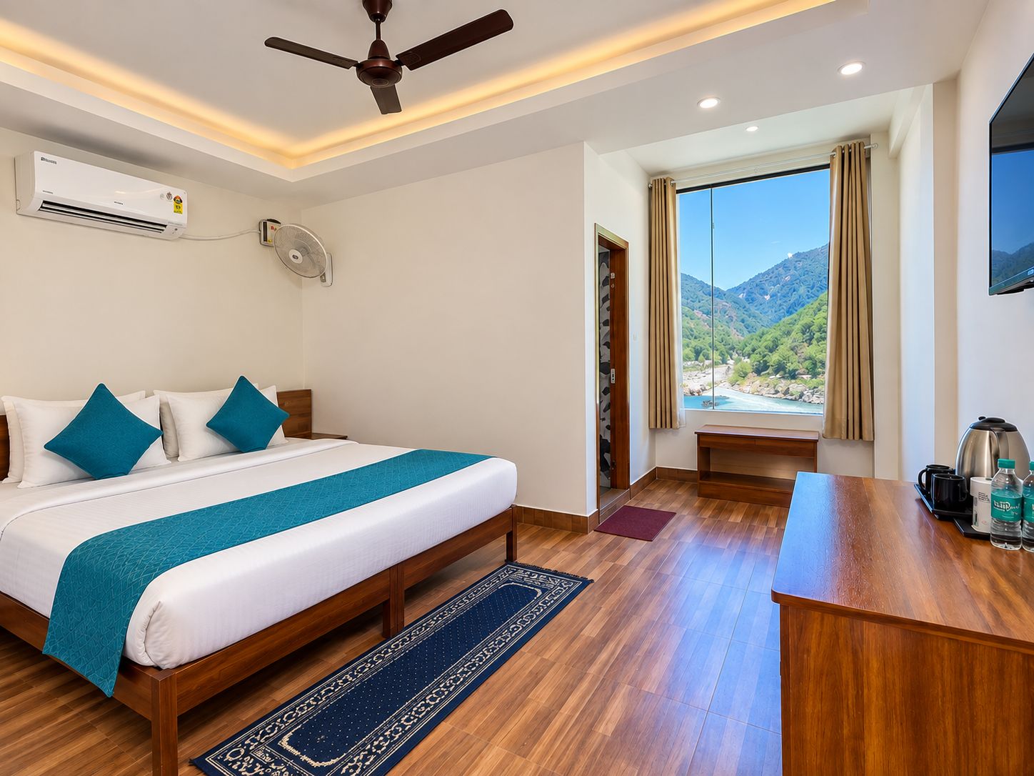 Quarto de hotel com cama, escrivaninha, cafeteira e vista para uma paisagem montanhosa.