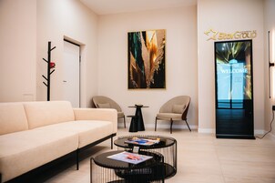Um lobby de hotel moderno com um sofá, duas cadeiras, uma mesa de centro, uma obra de arte na parede e uma tela de boas-vindas StarGroup.