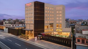 Um hotel moderno com um letreiro chamativo da marca 'RAMADA', vários andares e uma entrada bem iluminada.