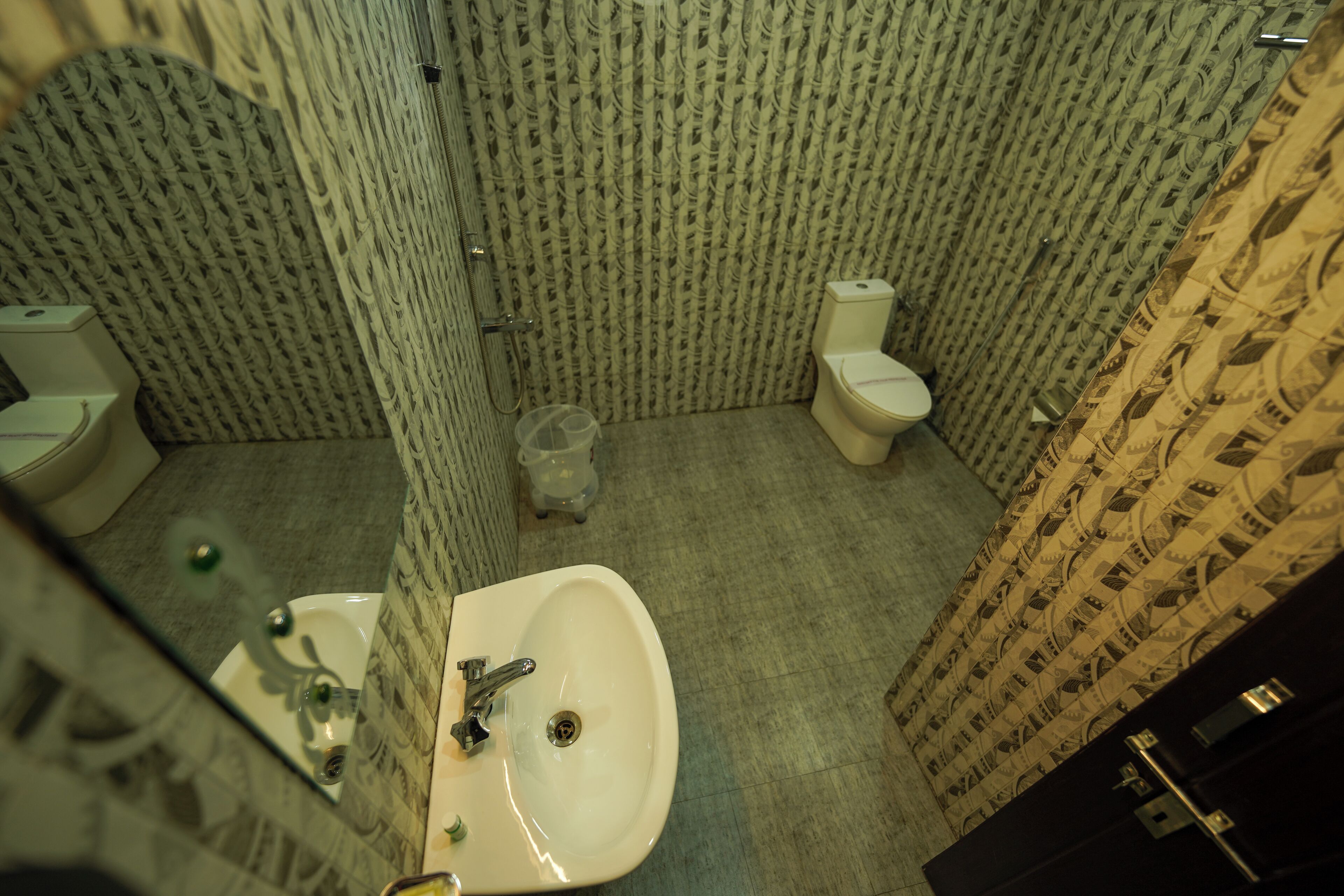 Casa de banho com papel de parede estampado, lavatório, sanita e zona de duche.