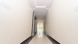 Um corredor comprido e estreito com piso brilhante, iluminação embutida e vista para área externa verde através de uma porta de vidro no final.