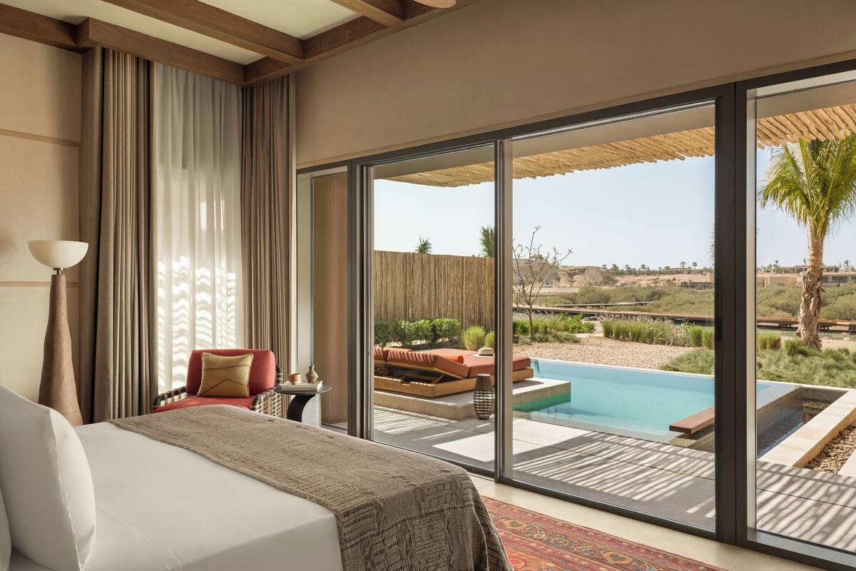 Quarto com cama grande, vista para piscina ao ar livre e porta de vidro deslizante para um espaço de pátio.