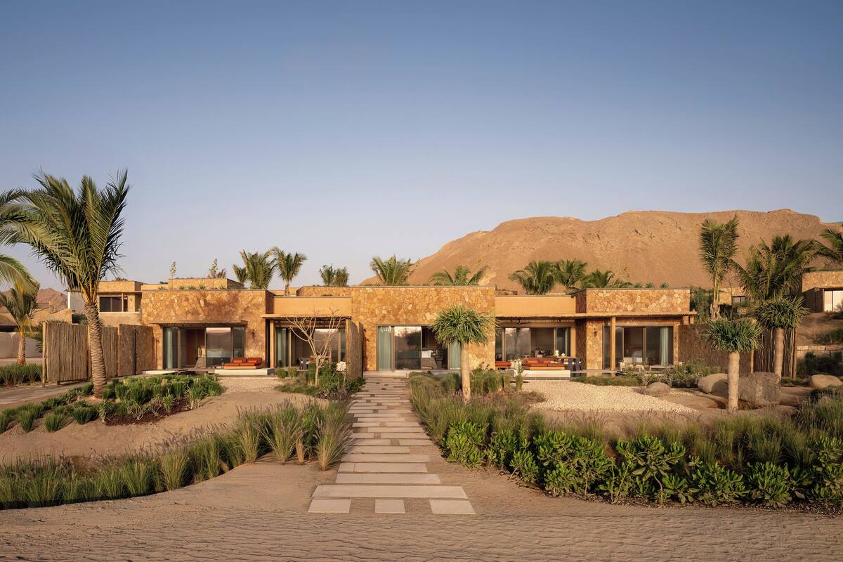 Um resort no deserto com várias villas, um caminho pavimentado e palmeiras.