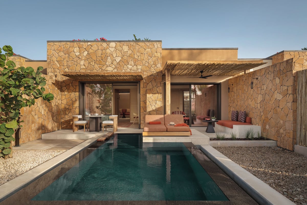 Uma área moderna de piscina ao ar livre, com paredes de pedra, um espaço de estar com sofá e cadeiras, e uma mesa de jantar.