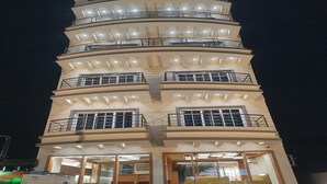 Hotel com vários andares, varandas em cada pavimento, grandes janelas e fachada bem iluminada.