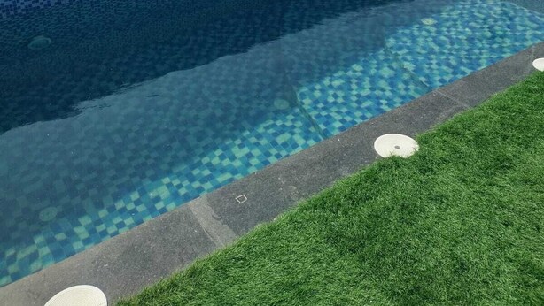 Piscina com borda em mosaico azul, área gramada e vista para o oceano.