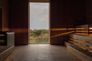 Quarto com uma janela grande, paredes de madeira, um banco e uma mala.