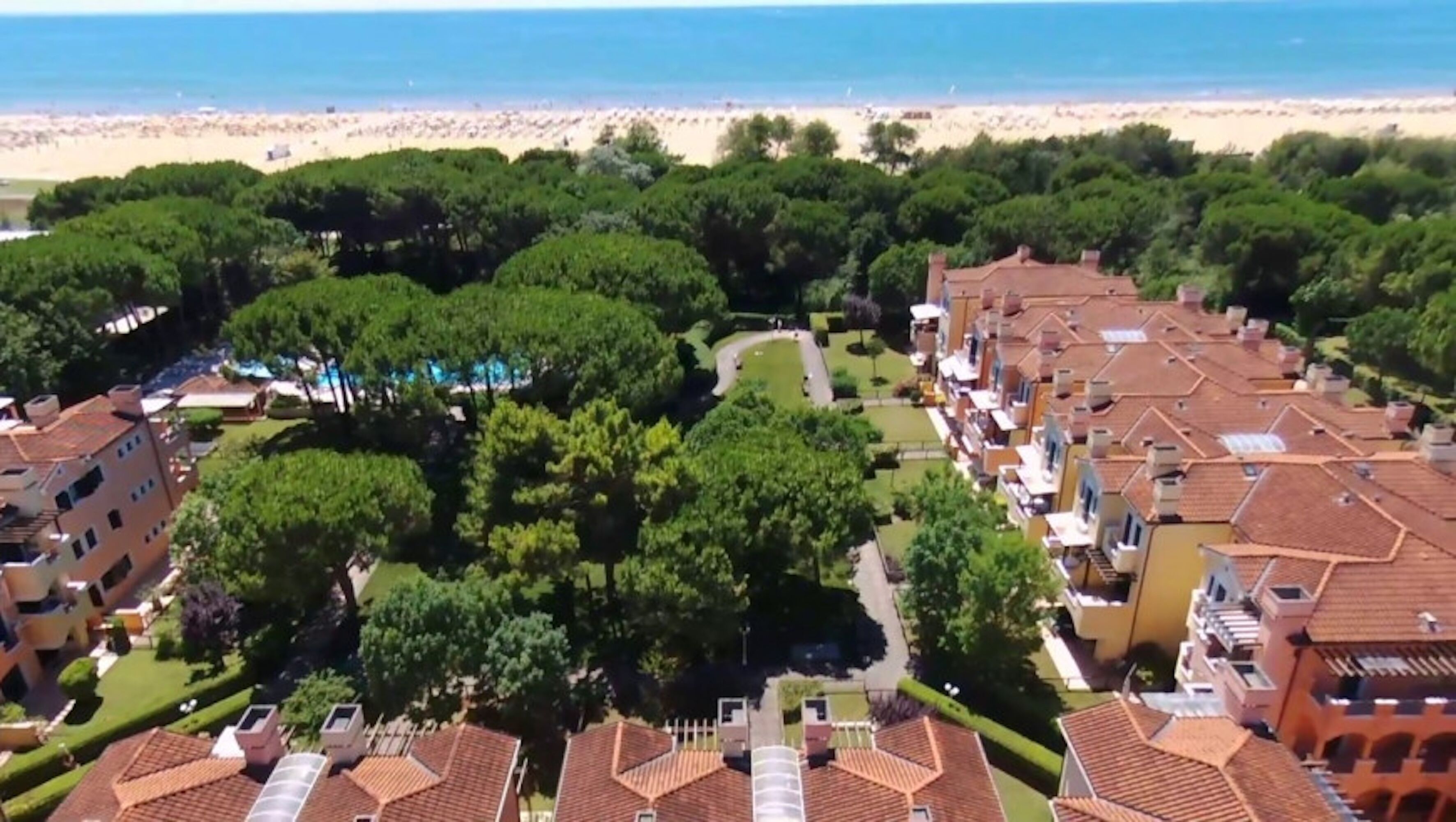 Uma área residencial costeira com casas em socalcos, um caminho central e uma praia ao fundo.