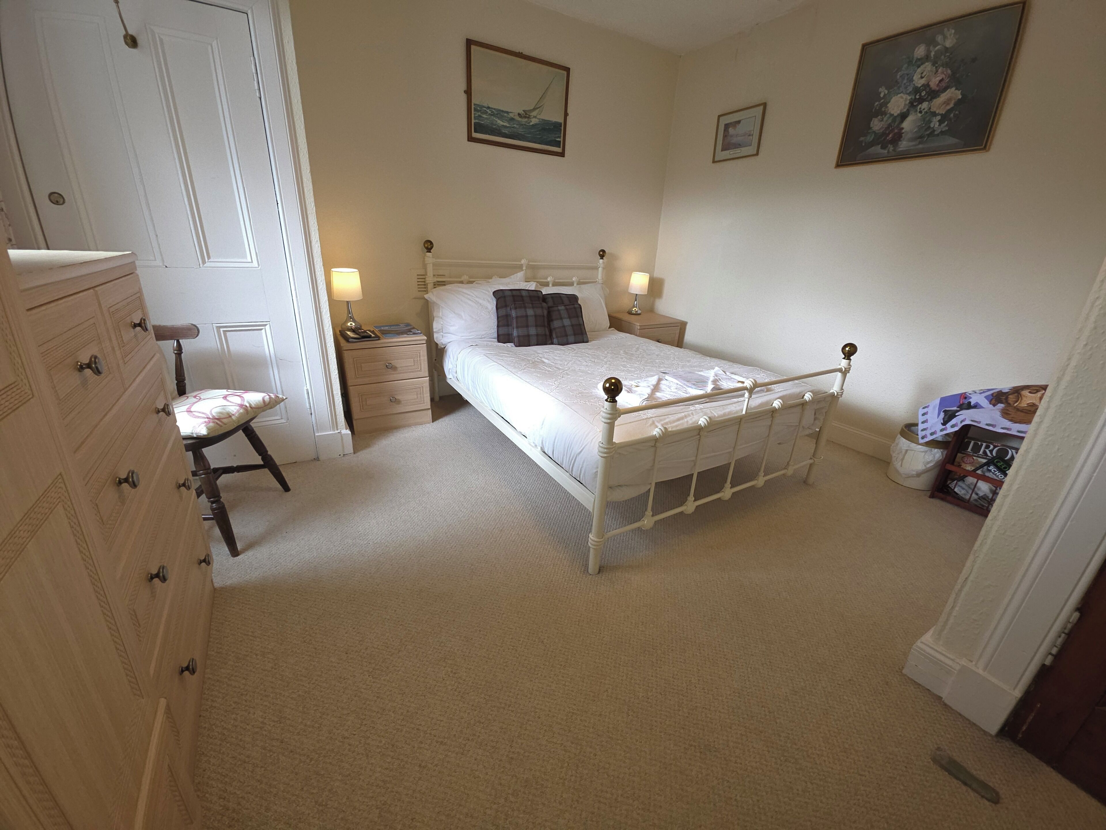 Quarto com cama, cômoda, mesas de cabeceira, luminárias e quadros na parede.