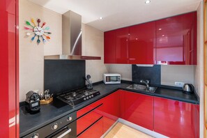 Uma cozinha moderna com armários vermelhos, bancada preta, eletrodomésticos de aço inoxidável e um relógio de parede exclusivo.