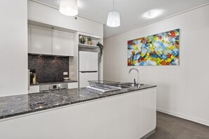 Cozinha moderna com armários brancos, bancada de granito e um quadro abstrato colorido na parede.