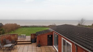 Uma área de pátio com vista para o mar, um edifício de tijolos e móveis de exterior.