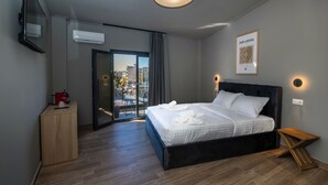 Quarto de hotel moderno com uma cama grande, uma TV de tela plana, uma mesinha de madeira e um quadro emoldurado na parede.
