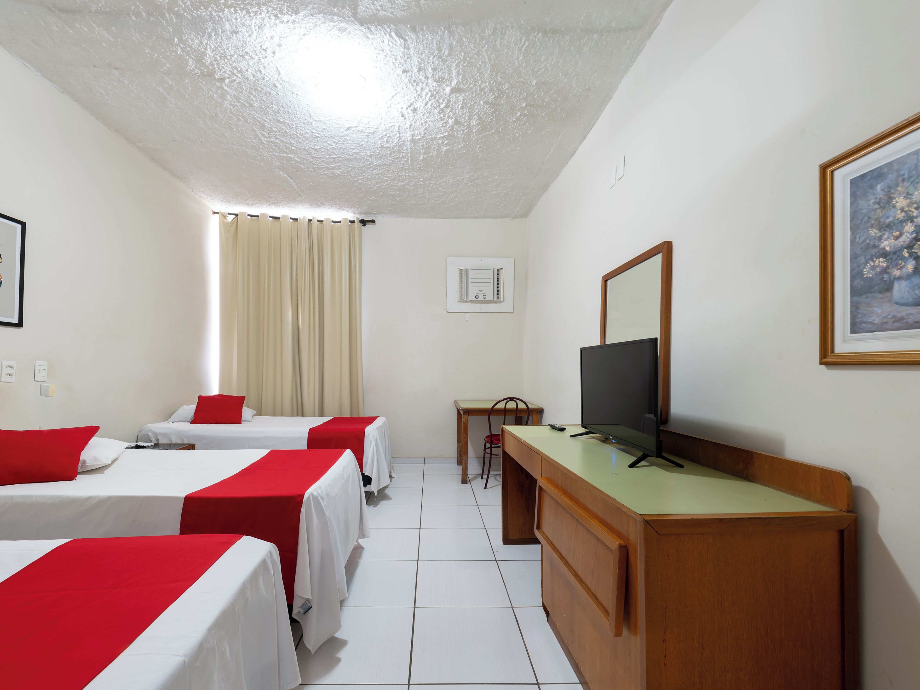 Quarto de hotel com duas camas, uma escrivaninha, uma cadeira, uma televisão e um quadro na parede.