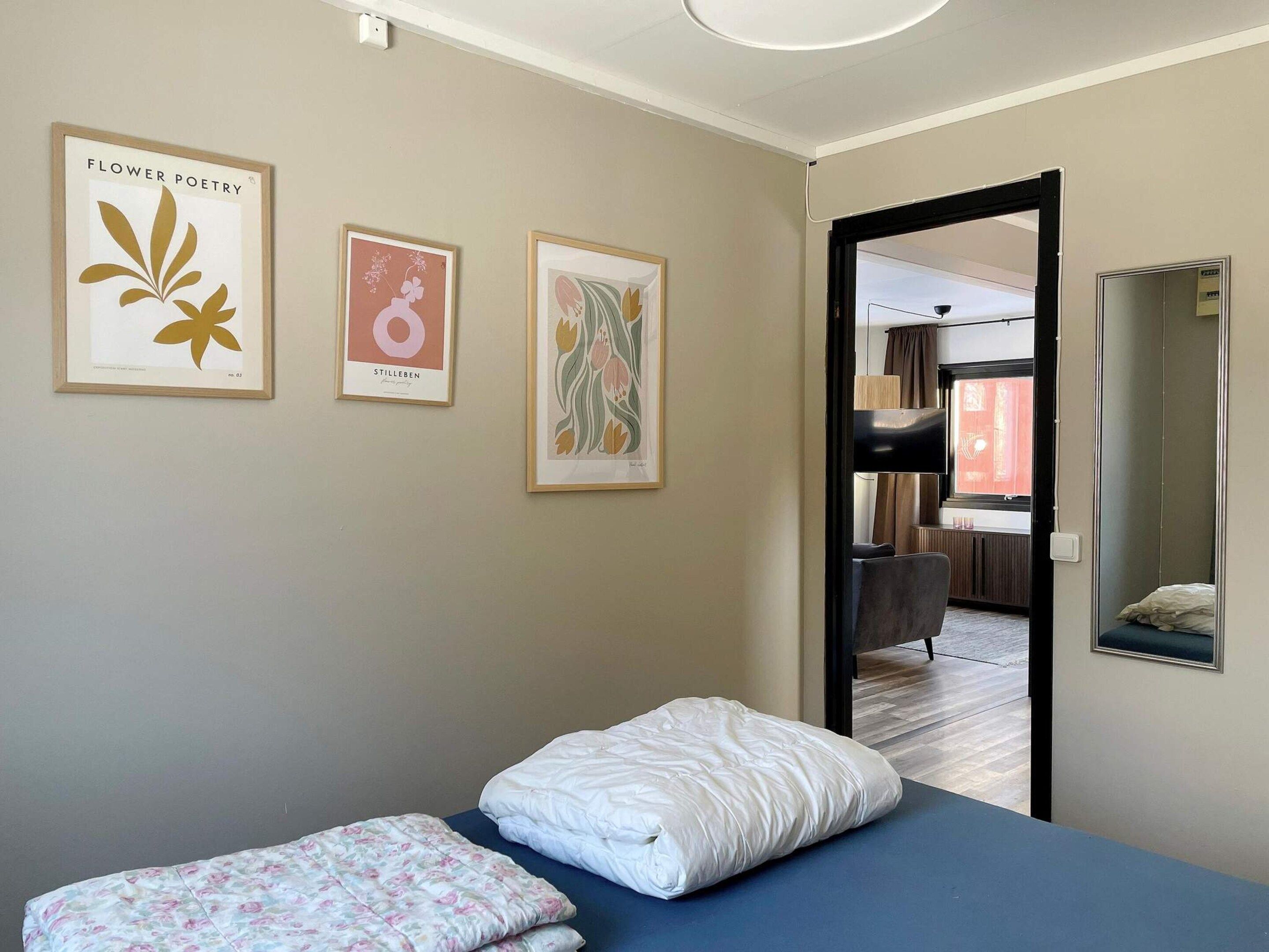 Quarto de hotel com cama, colchão azul, colcha estampada e três obras de arte emolduradas na parede.