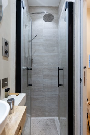 Um box de chuveiro moderno com porta de vidro, chuveiro manual e piso revestido com azulejos.