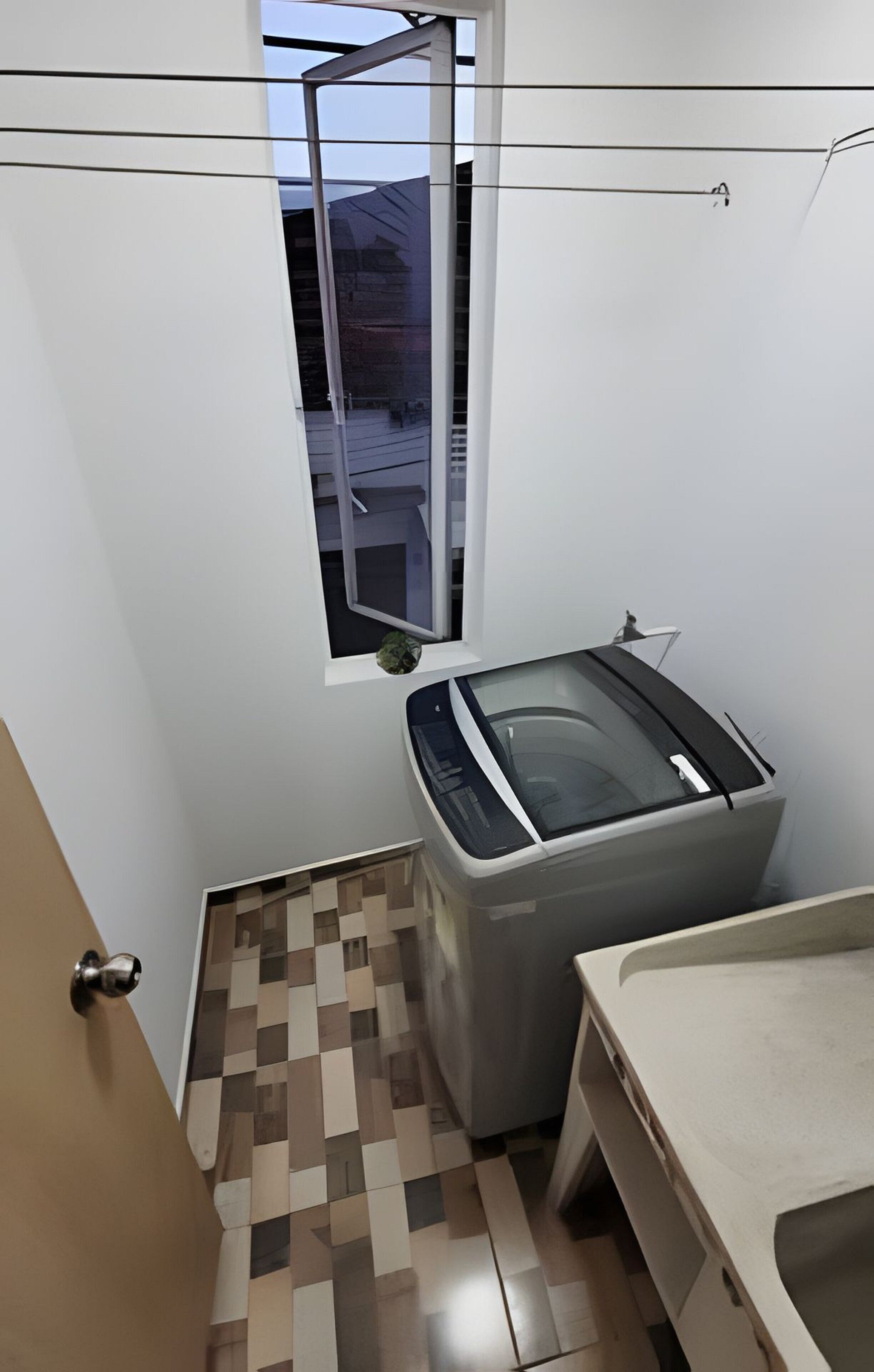 Quarto compacto com máquina de lavar, uma pequena mesa e uma porta com puxador.