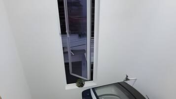 Quarto compacto com máquina de lavar, uma pequena mesa e uma porta com puxador.