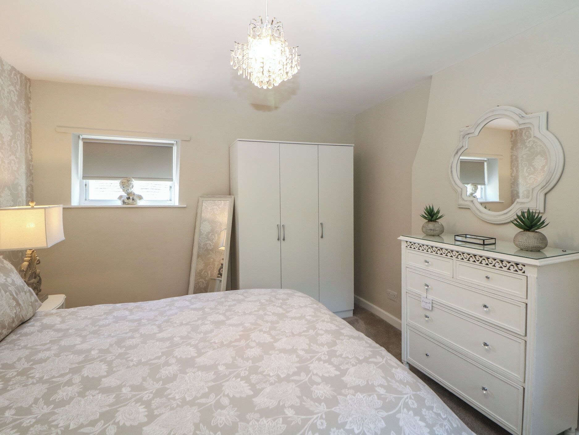Quarto com cama, penteadeira, espelho, janela e um candelabro.