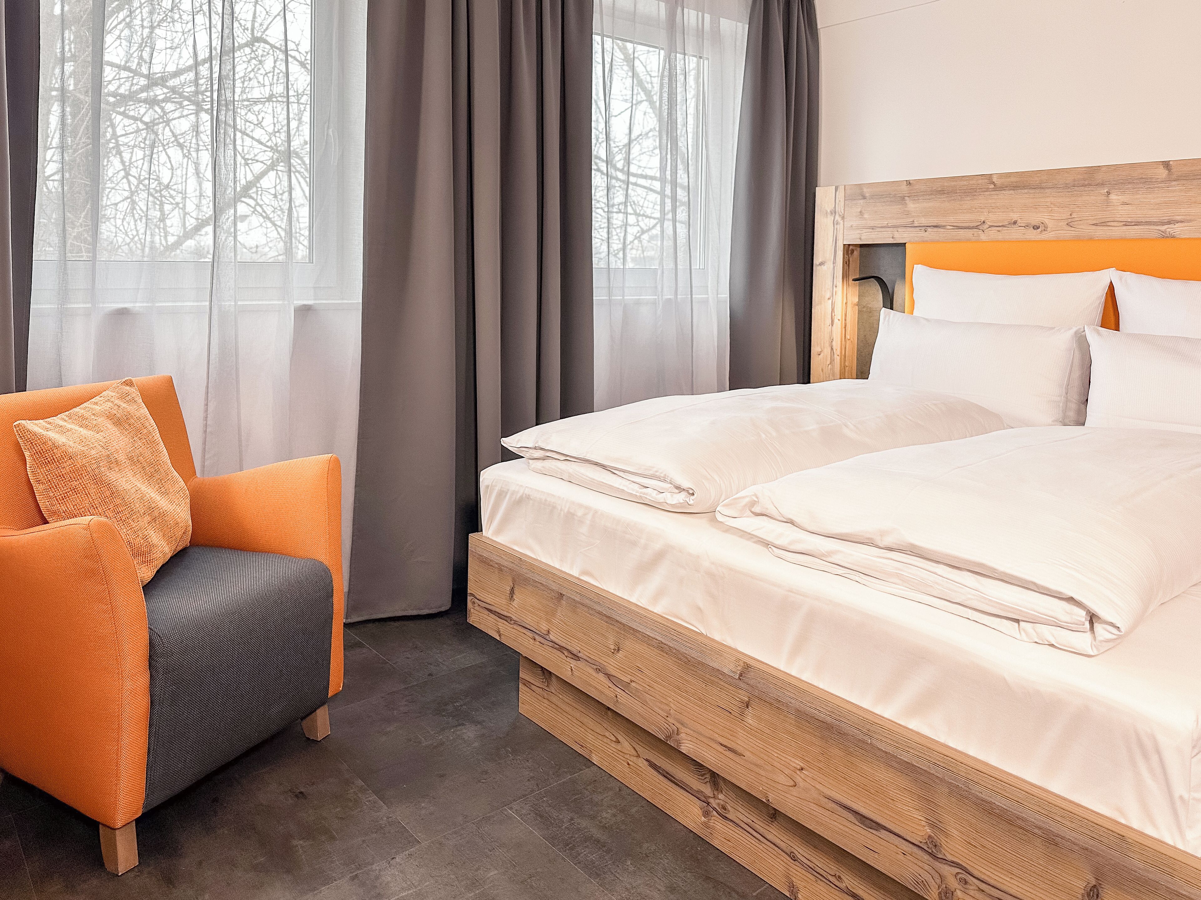 Quarto de hotel com uma cama, uma cadeira e uma janela com cortinas.