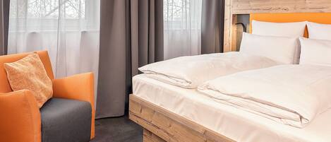 Quarto de hotel com uma cama, uma cadeira e uma janela com cortinas.
