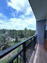 Uma varanda com vista para uma paisagem exuberante, incluindo palmeiras e uma casa ao longe.