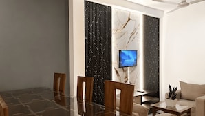 Uma sala de estar moderna com mesa de jantar de vidro, cadeiras de madeira, sofá, televisão e ventoinha de teto.
