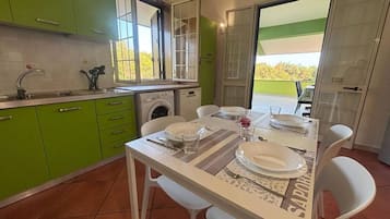 Uma cozinha compacta com armários verdes, máquina de lavar embutida e área de jantar com mesa posta para quatro pessoas.