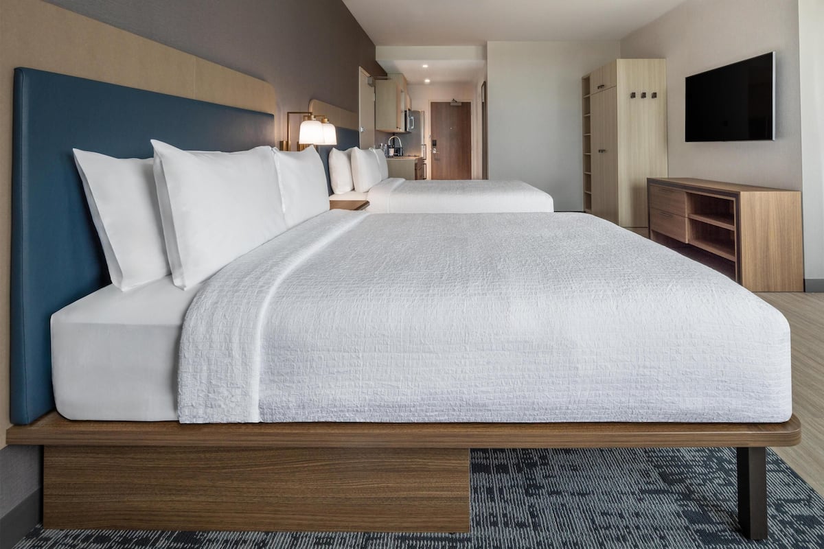 Quarto de hotel com uma cama grande, televisão, escrivaninha e guarda-roupa.