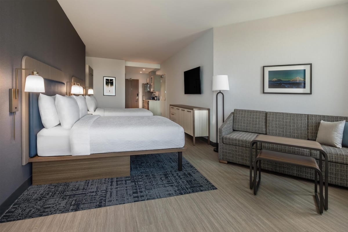 Quarto de hotel com cama, sofá, mesa de centro, televisão e um quadro na parede.